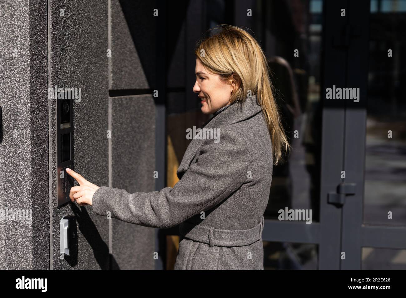 Happy woman ringing on doorbell at building entrance. Using intercom ...