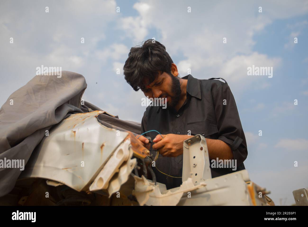 A mechanical worker repairing an old and damaged vehicle in an open ...
