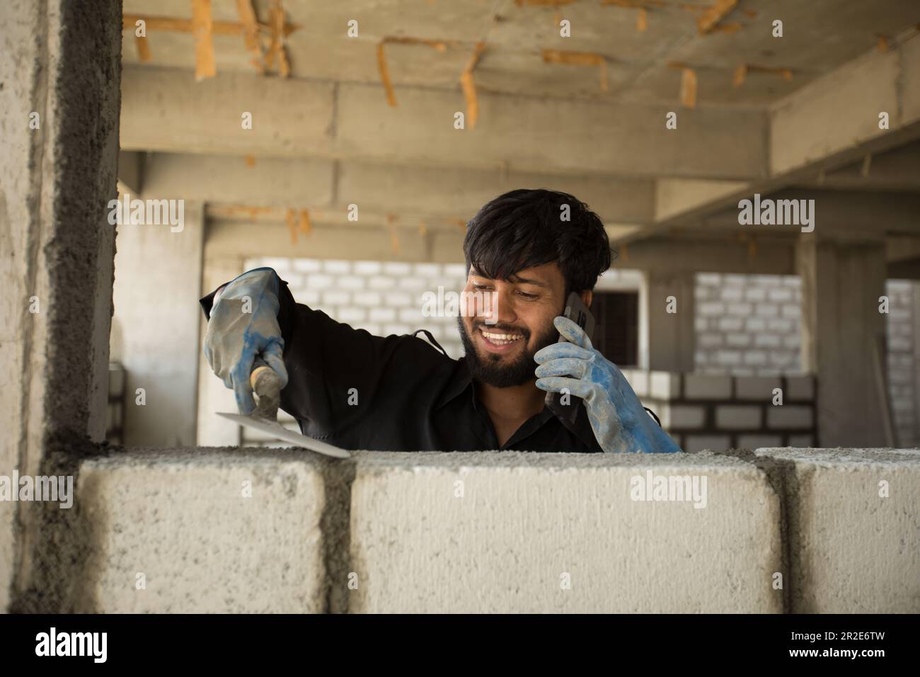 A happy construction labour builds a cement brick wall while talking on ...