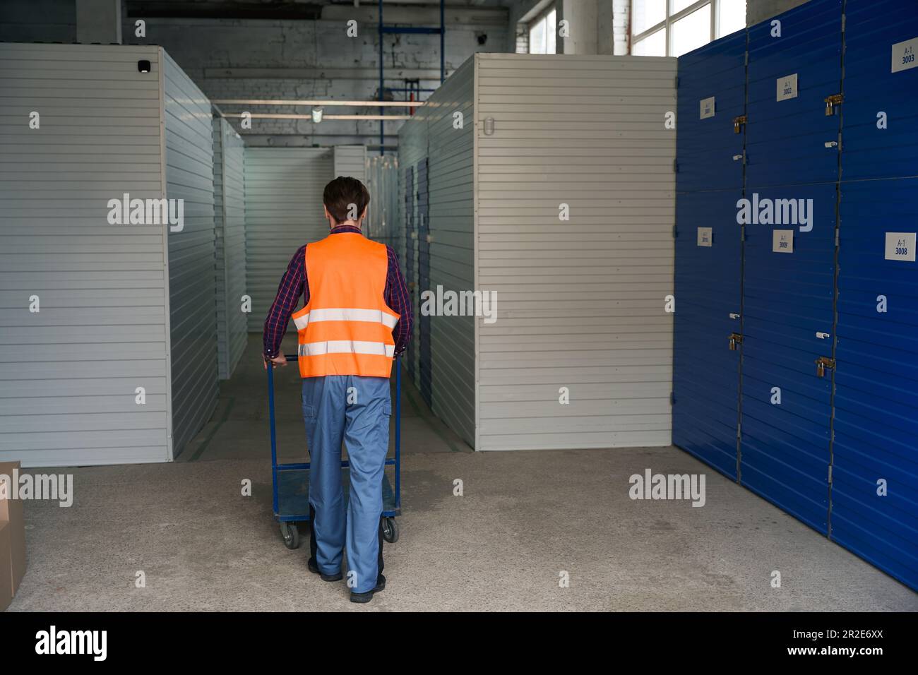 Back view of man in work clothes with platform truck into warehouse ...