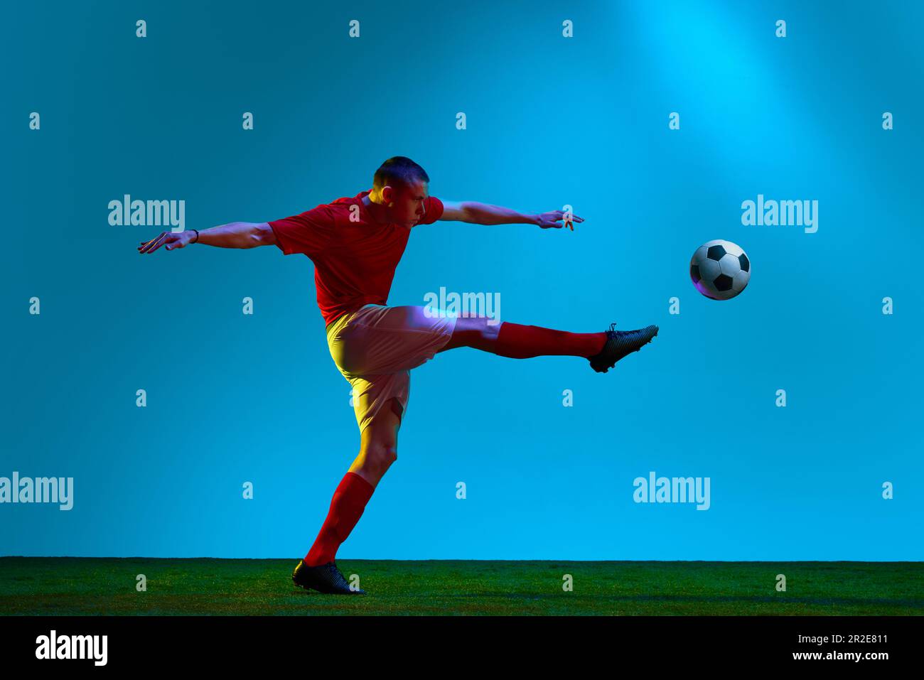 Portrait of soccer, football player in sports uniform kicking the ball ...