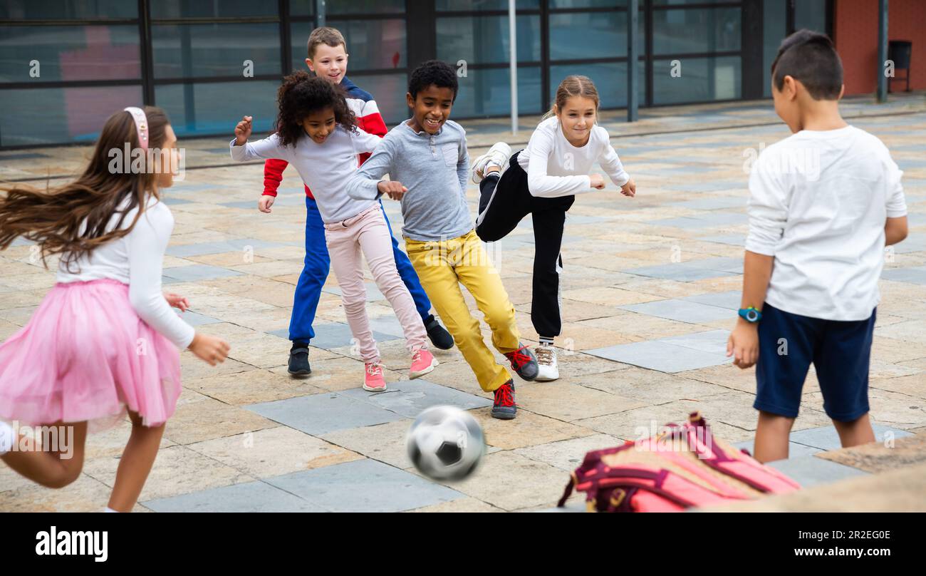 Cheerful tween schoolchildren playing with ball near school Stock Photo ...