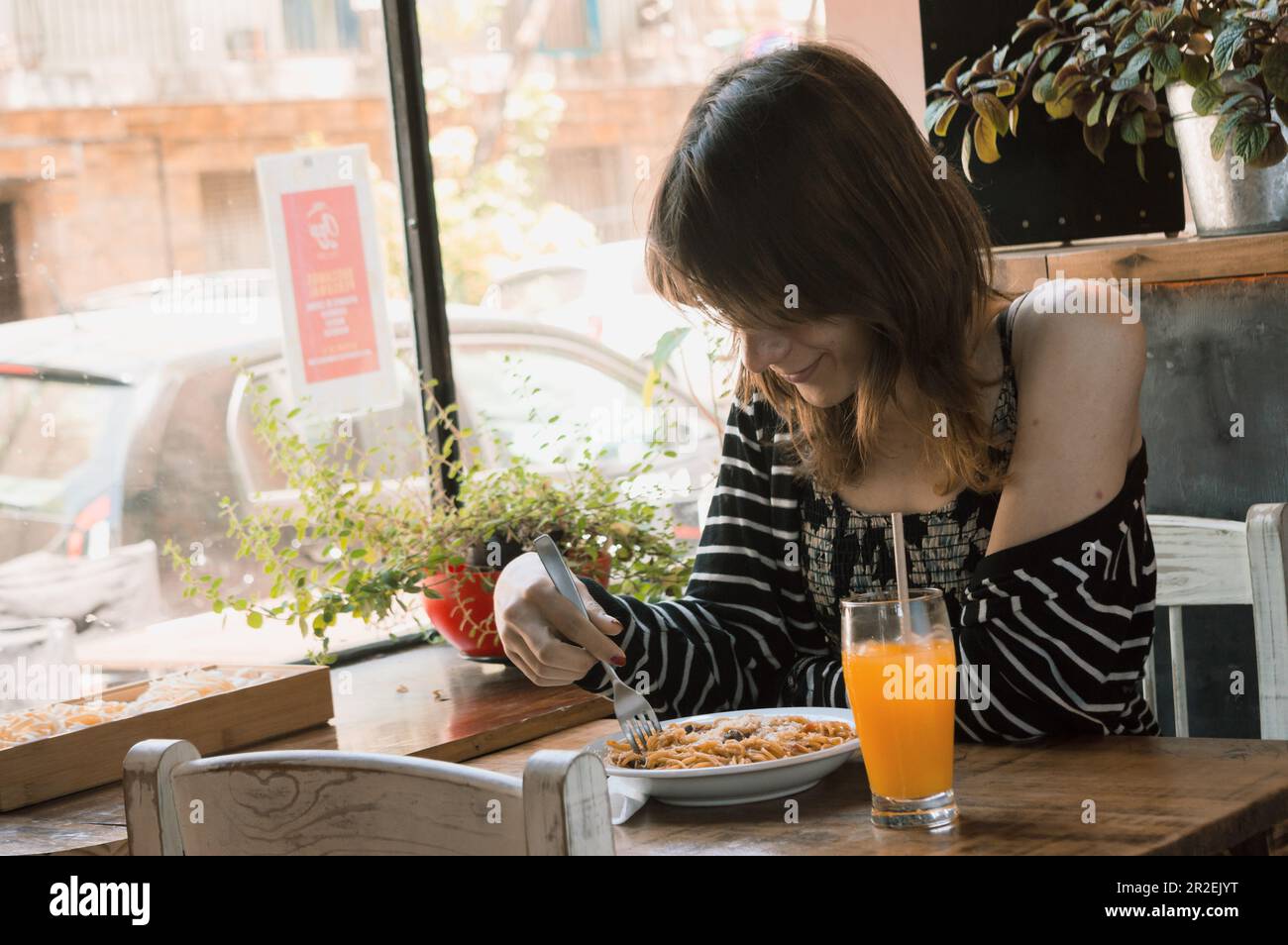 young transgender woman eating pasta with orange juice, sitting in a ...