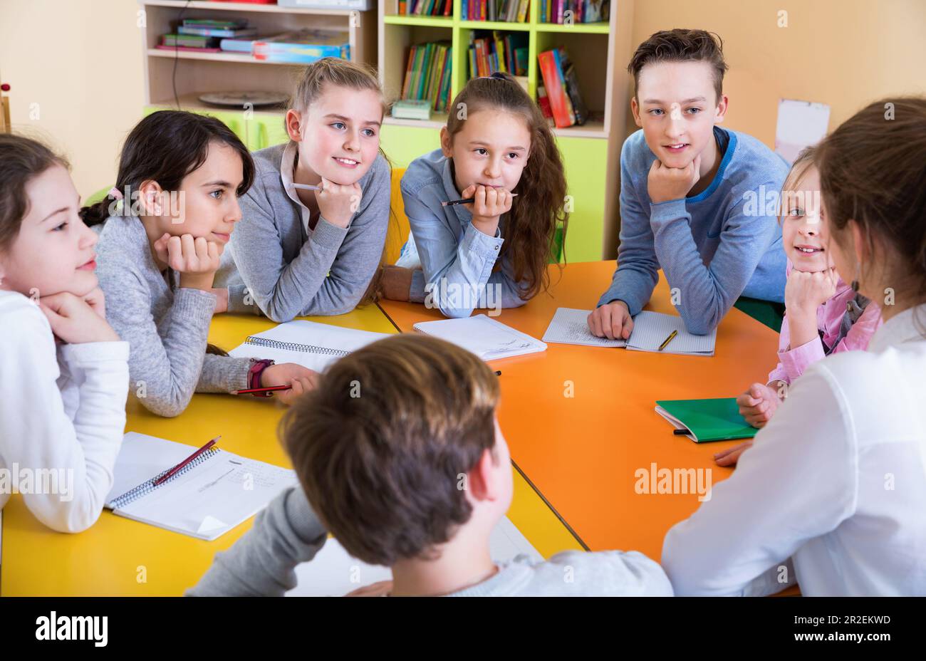 Friendly female teacher talking to children, sitting together around ...