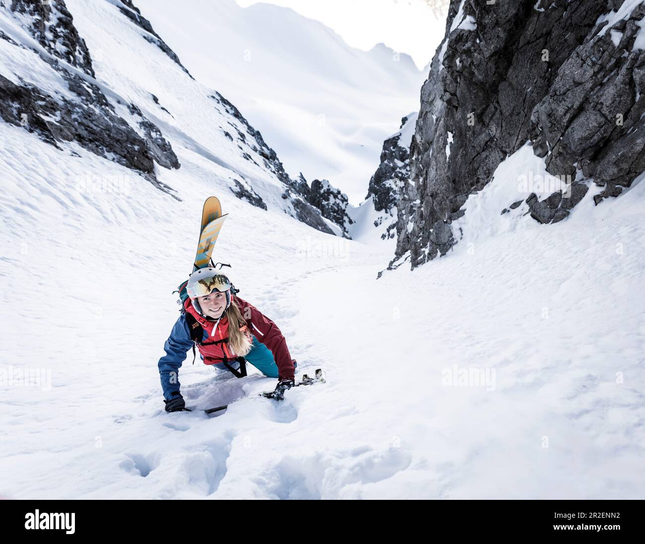 Ski alpinist ascending with skis from a backpack in a steep channel ...