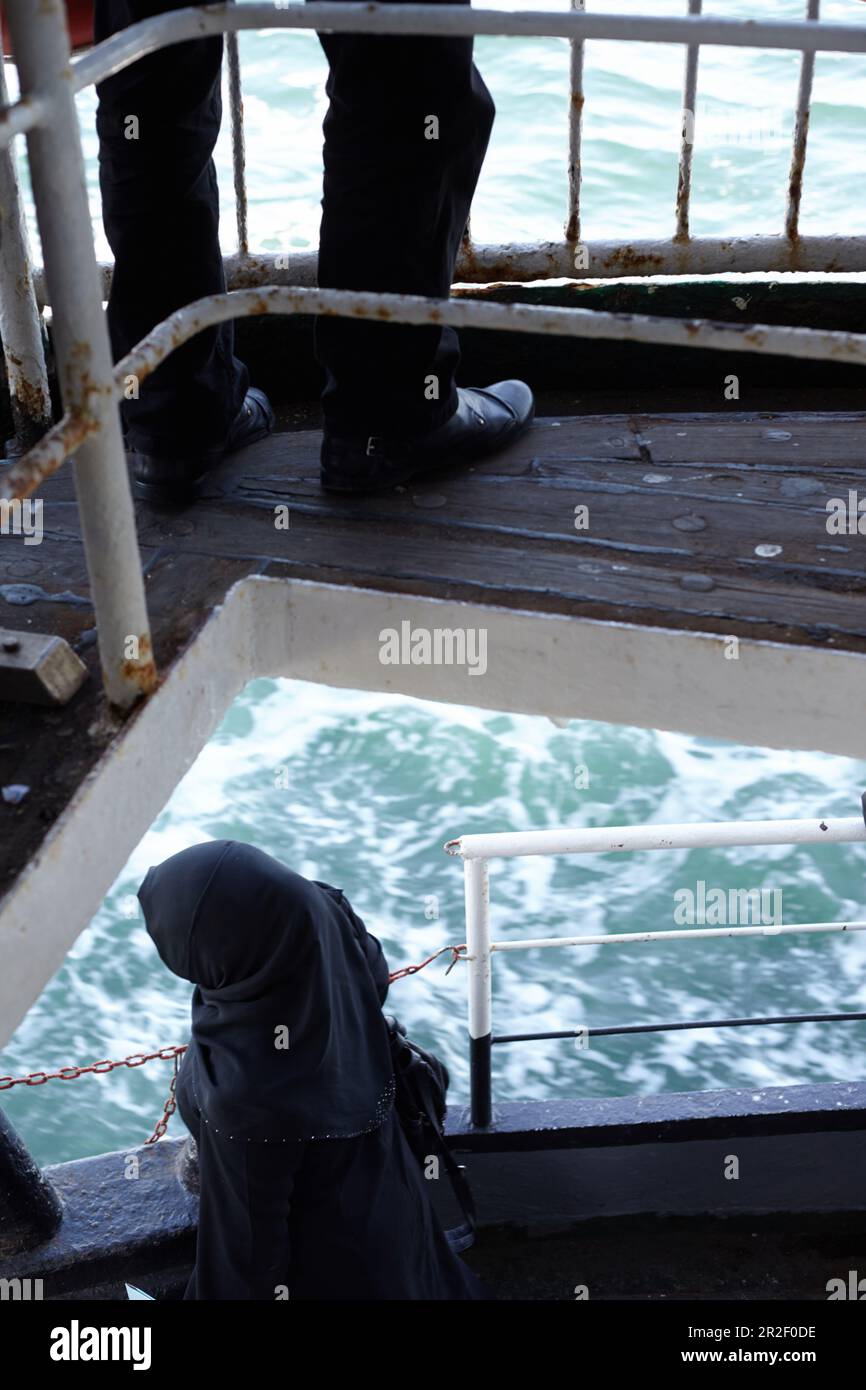 Male legs and the figure of a Muslim woman on the railing of the ferry ...