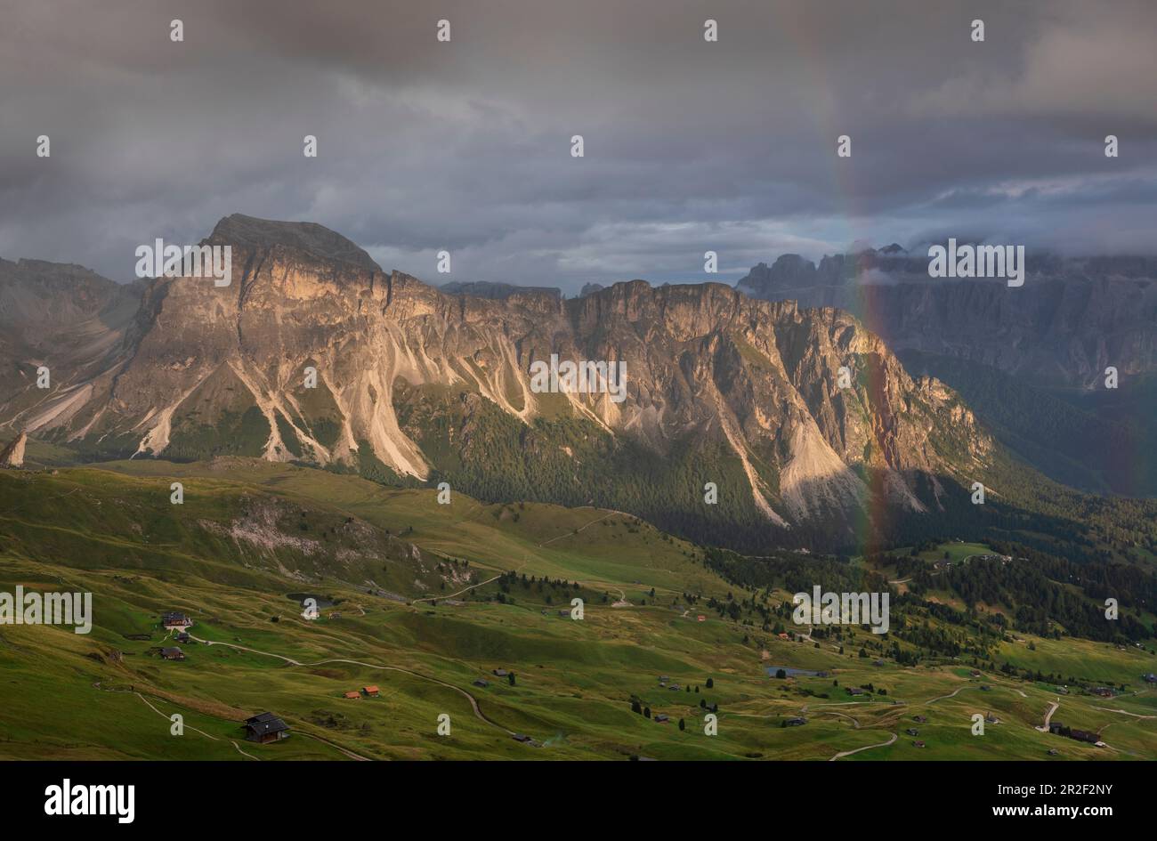 Mountain flank at Seceda with thick clouds, sun and rainbow in the ...