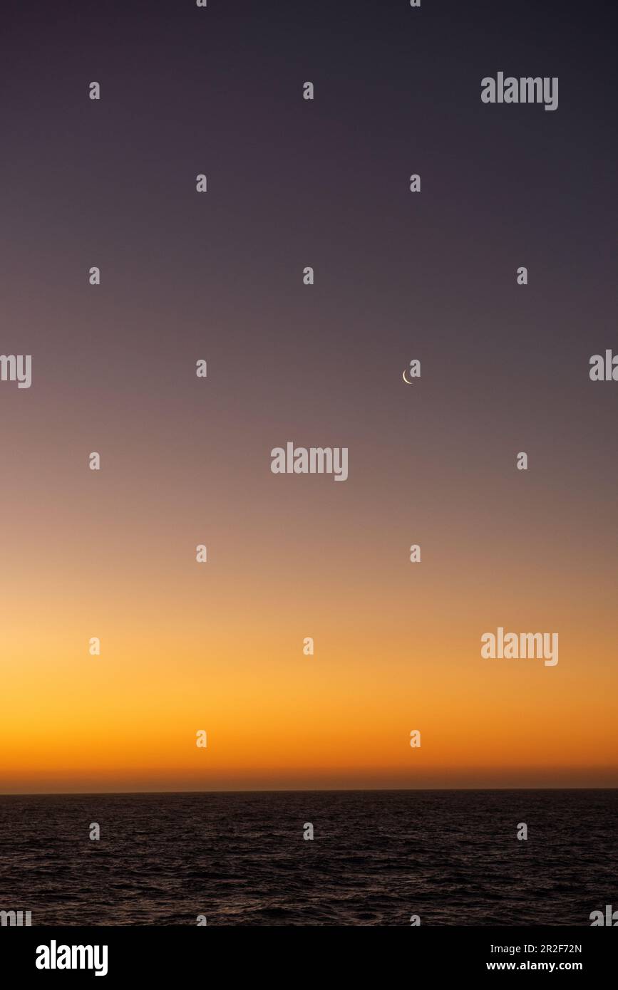 A crescent moon rises as the last warm glow of the sun fades on the ...