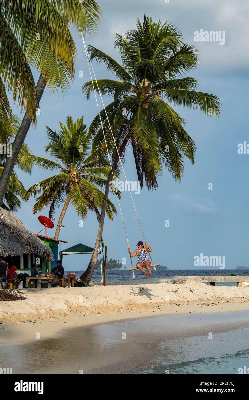A woman on a swing tied to a palm tree swings on the beach, Isla Aroma ...
