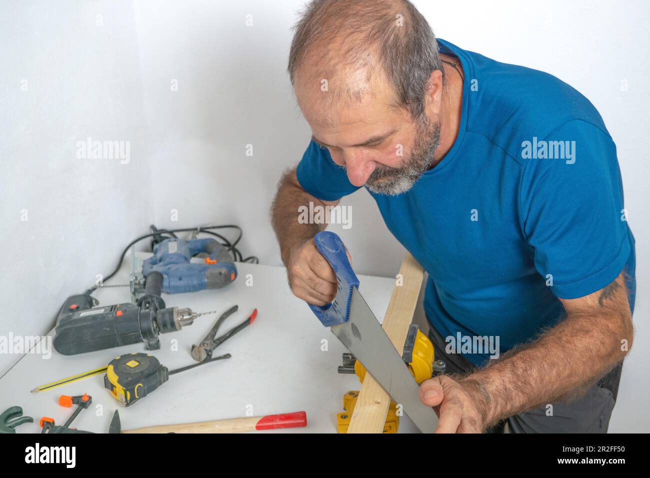 Front view of a male carpenter cutting wood in his workshop with a saw ...