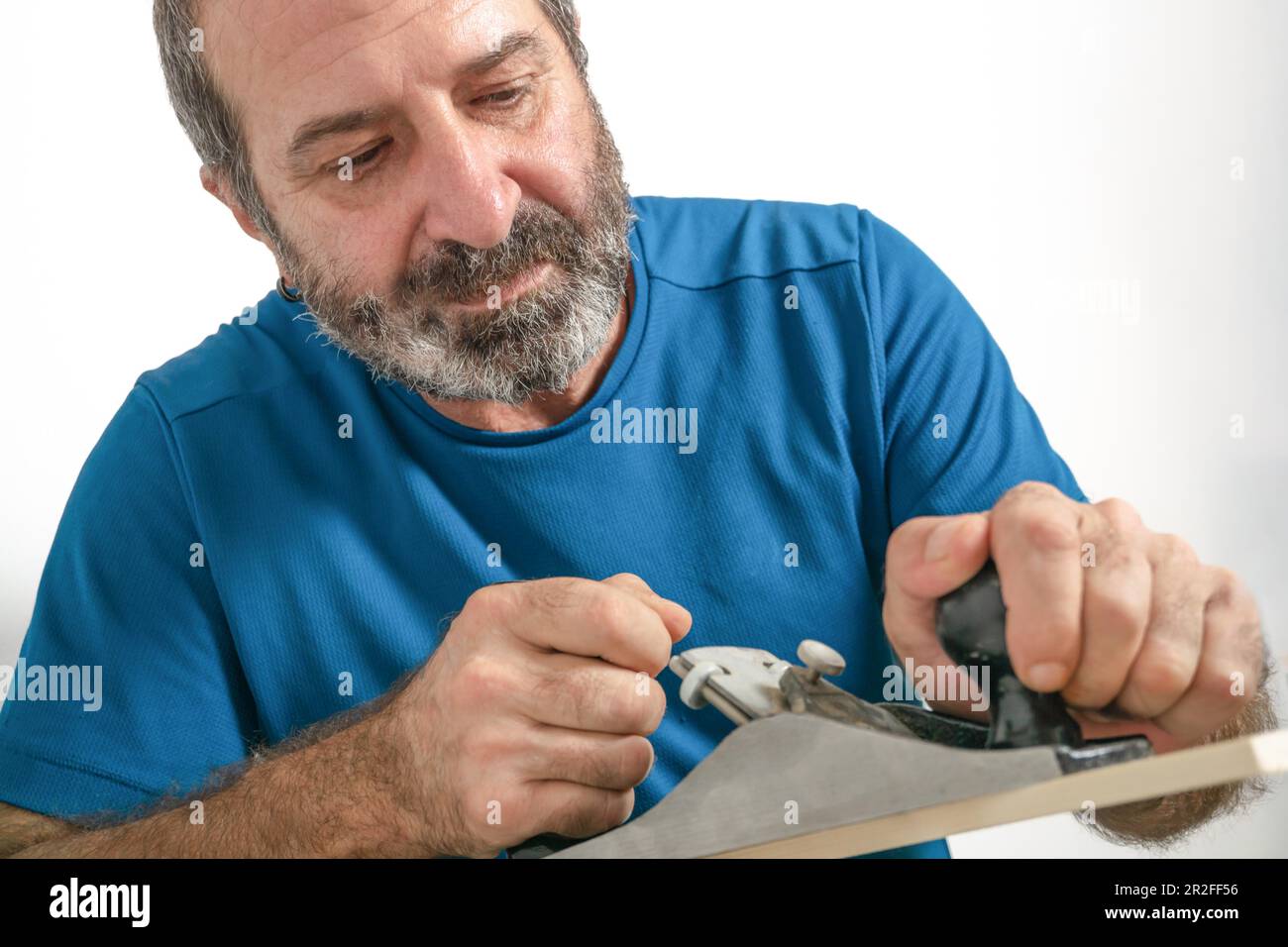 Front view of a bearded male carpenter planing wood with a hand planer ...