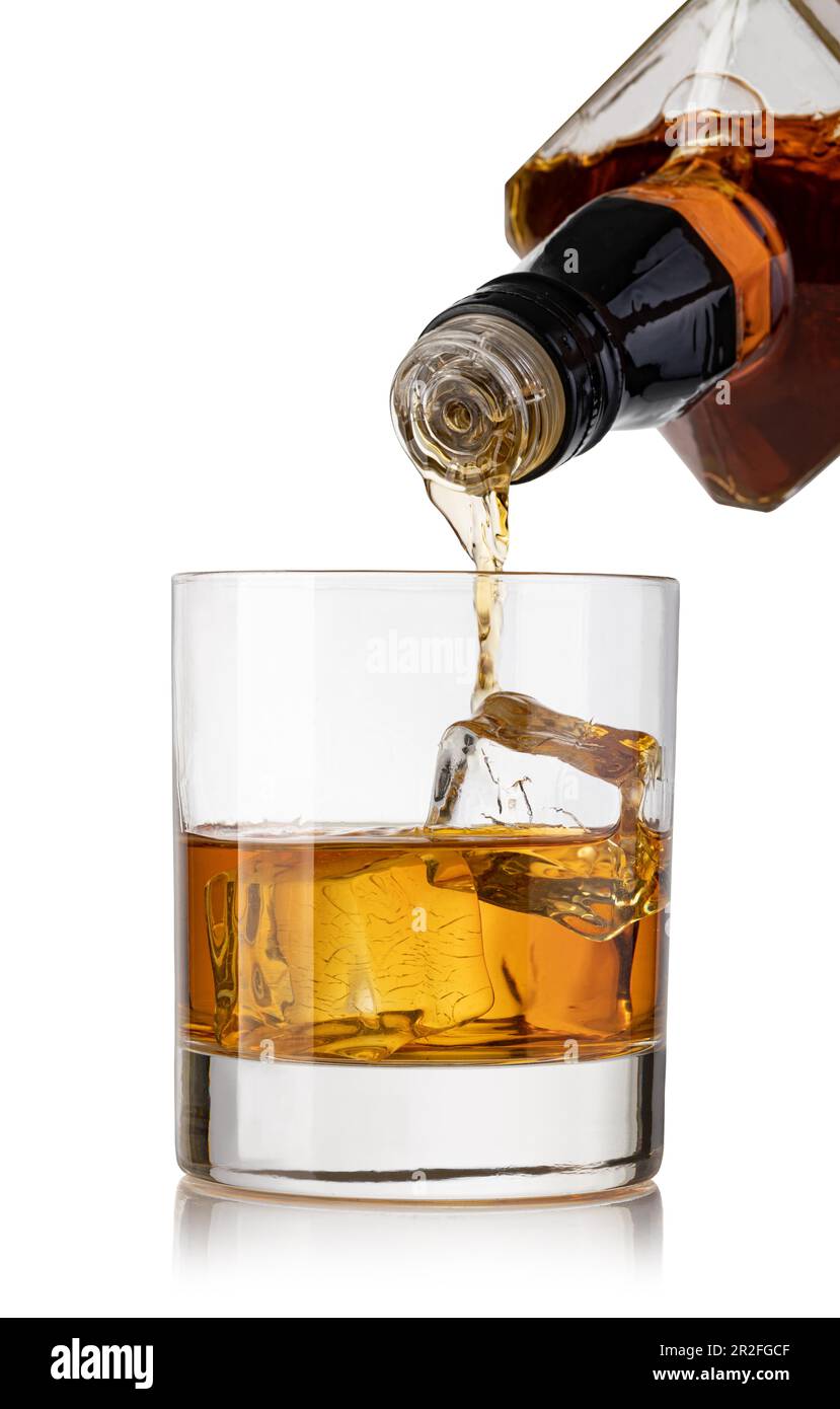 whiskey poured into a glass from a bottle isolated on a white ...