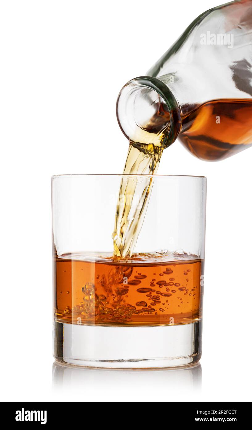 whiskey poured into a glass from a bottle isolated on a white ...