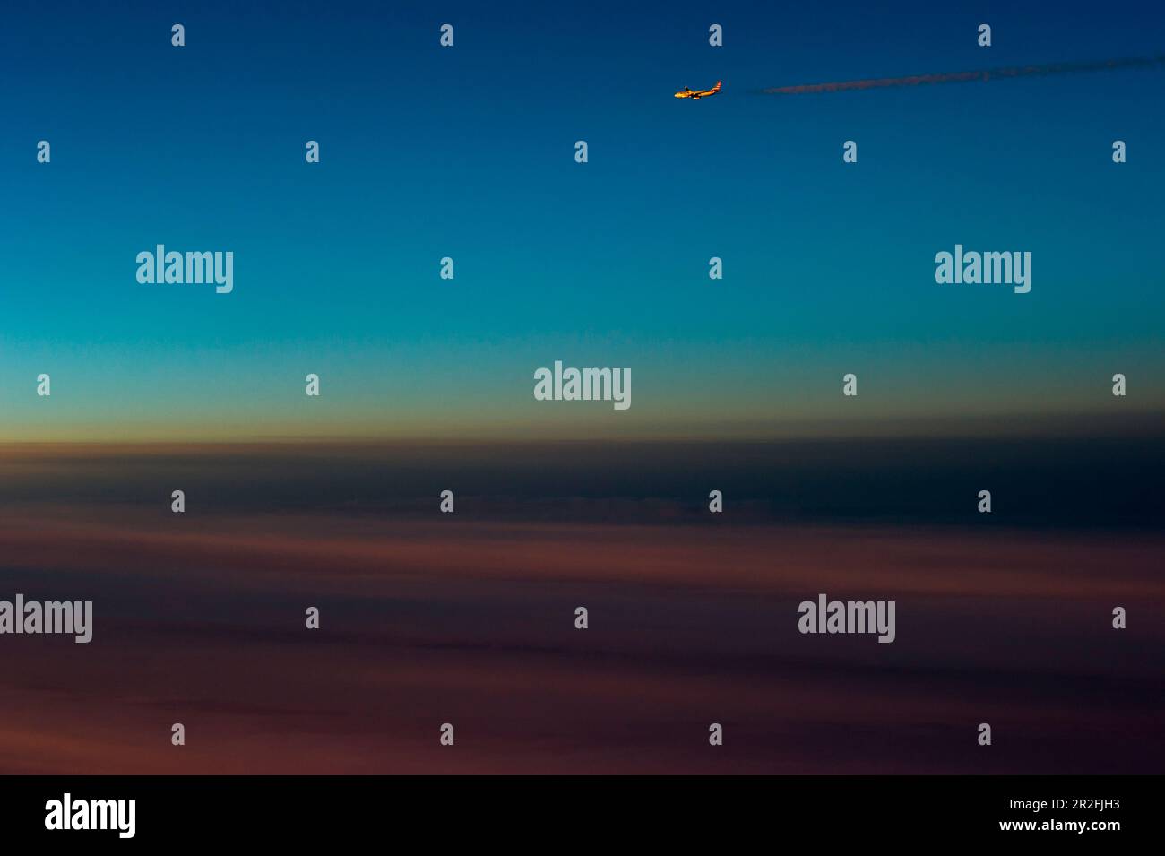 Airplane with contrails at dusk Stock Photo - Alamy