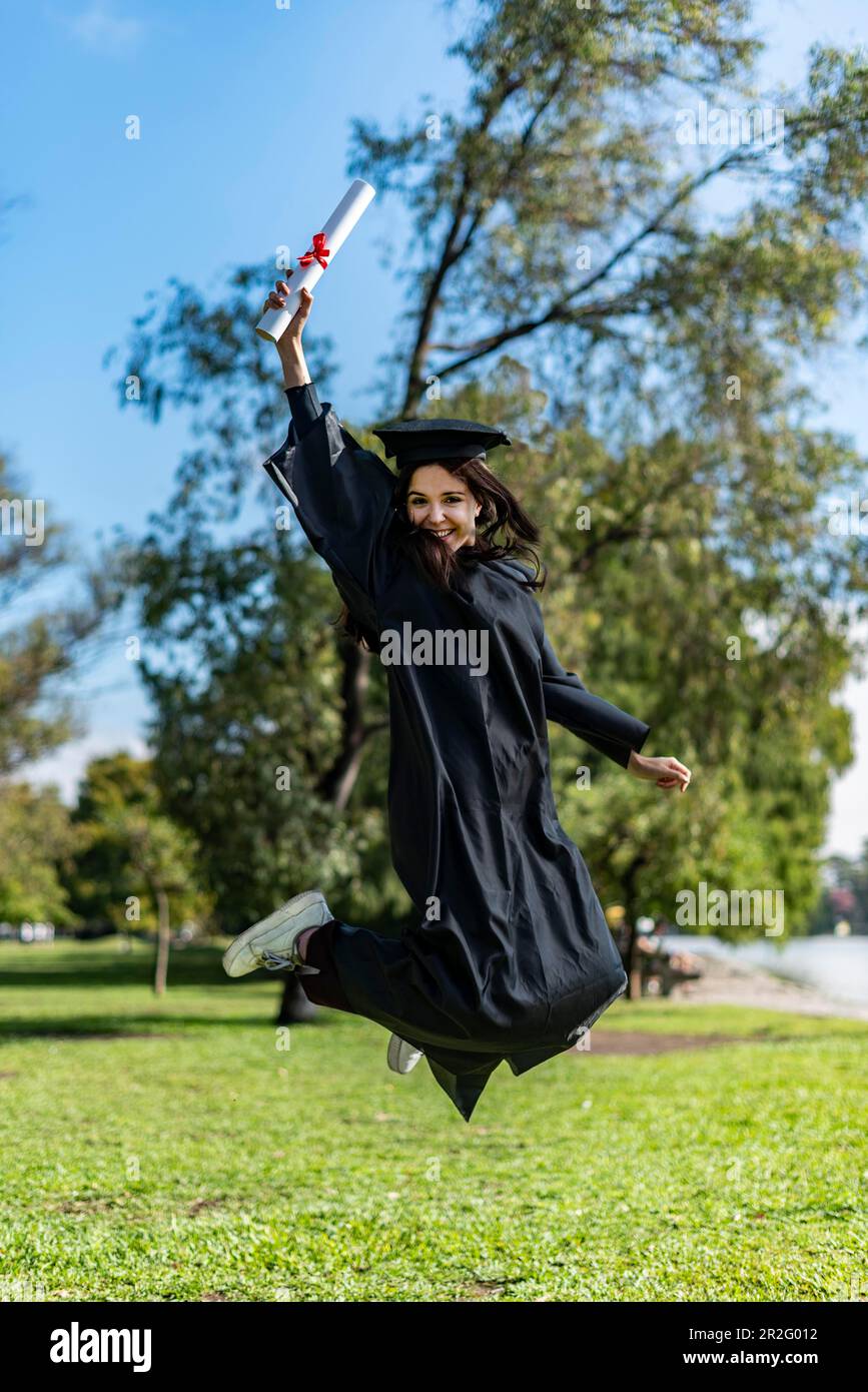 Happy graduated girl in a black gown jumping while holding her diploma ...