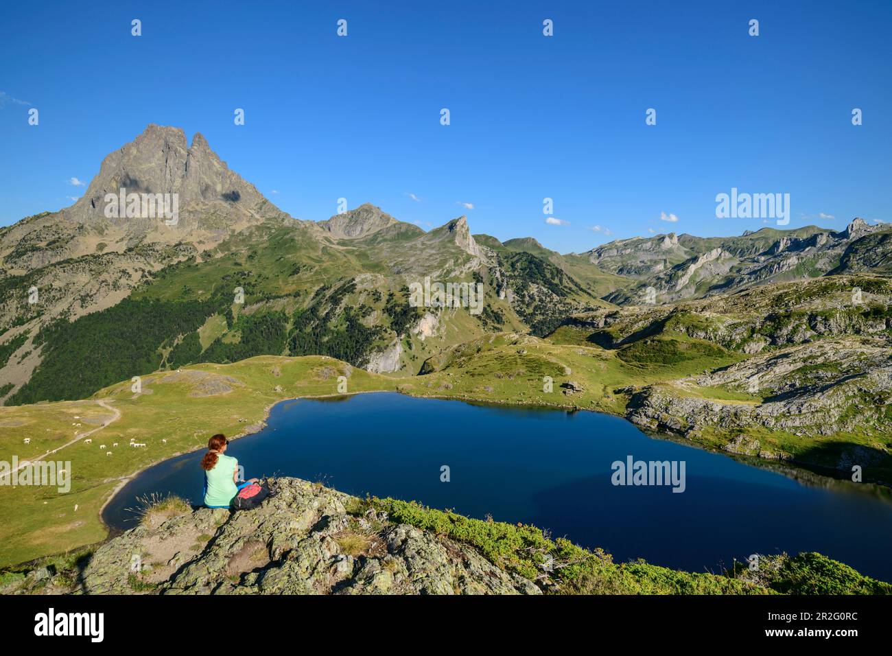 Woman while hiking sits on rock spur and looks at Lac Roumassot and Pic ...