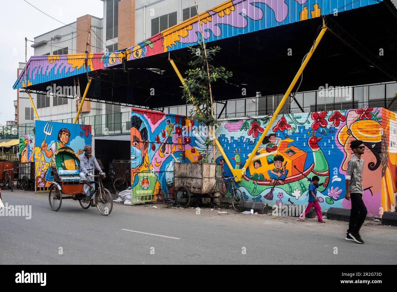 People walk past the graffiti in the waste transfer station of Mirpur ...
