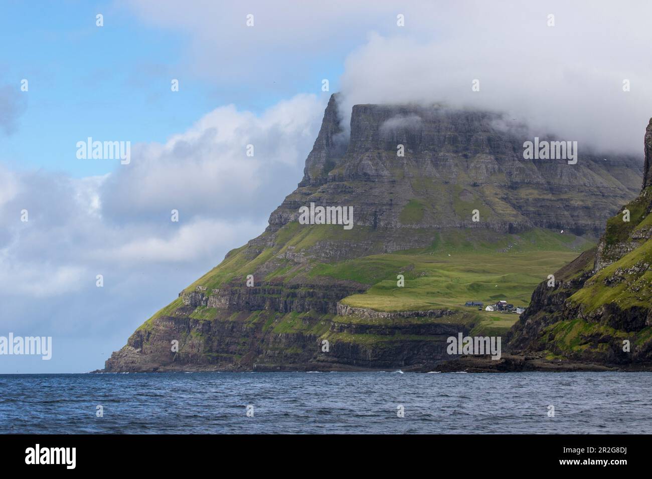 A few small houses on a cliff in front of a mountain backdrop ...