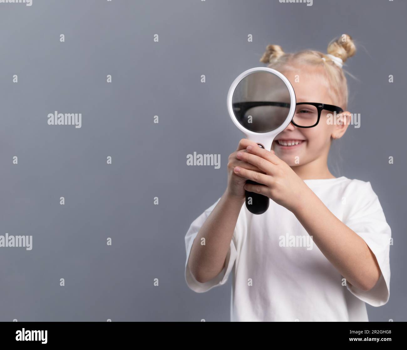 child looking through magnifying glass on gray background. Portrait of ...