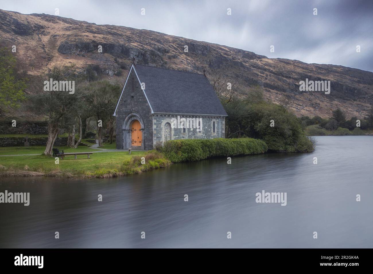 Small stone chapel with wooden door on the lake shore. mountain in the ...