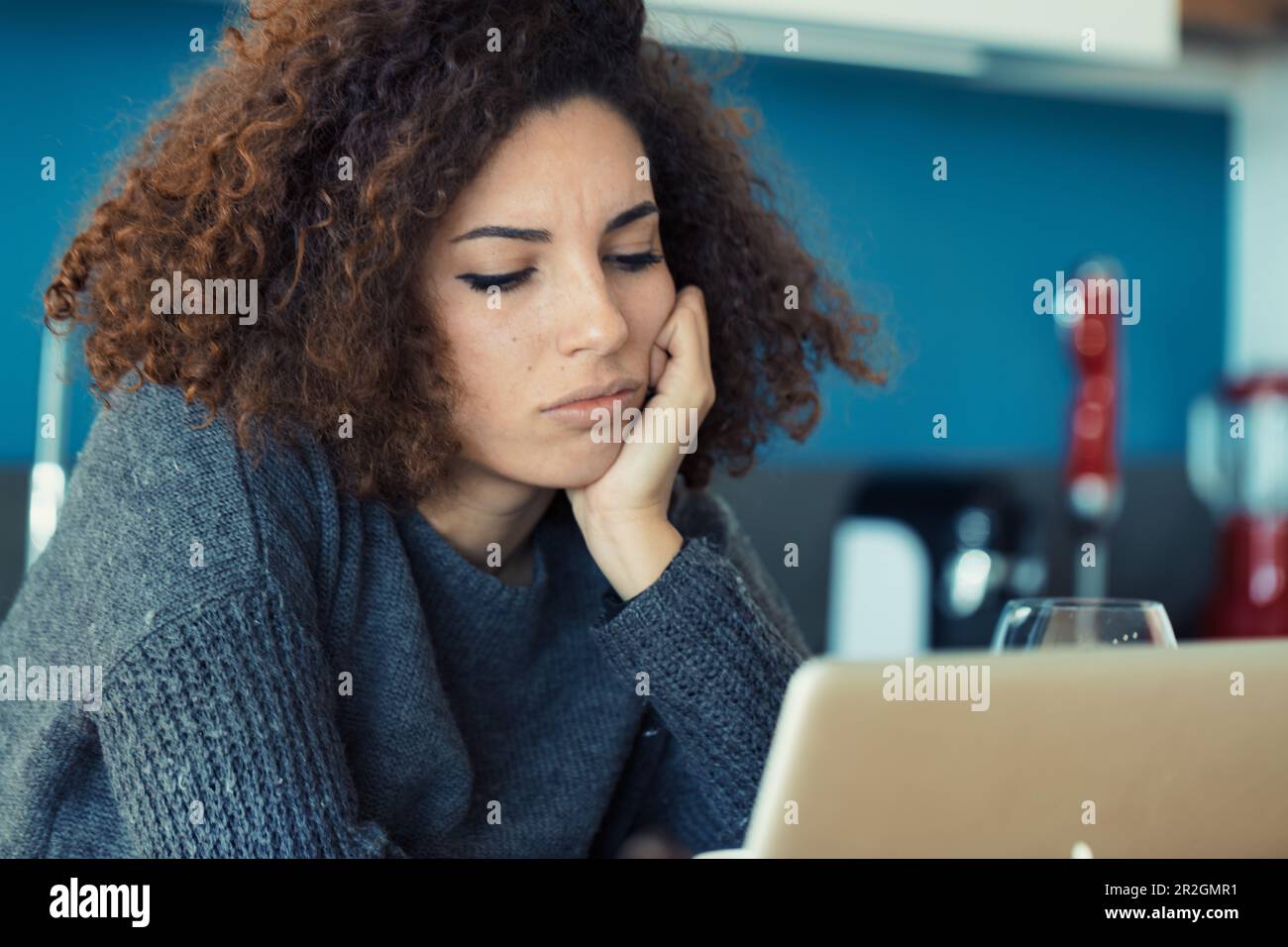 Annoyed woman frowns at her laptop screen in the kitchen. As a student ...
