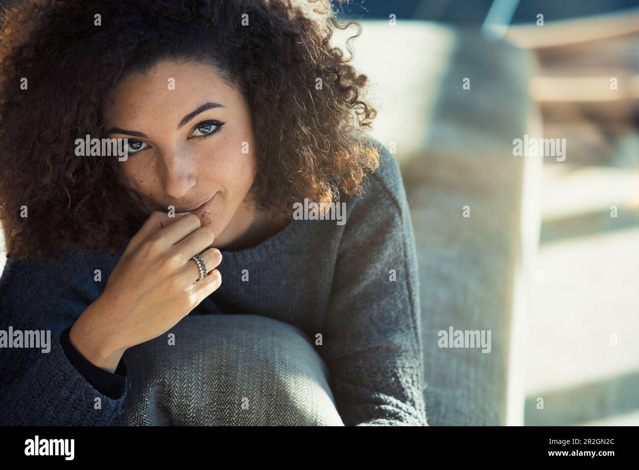 In her sunlit living room, a curly-haired young model lounges on her ...