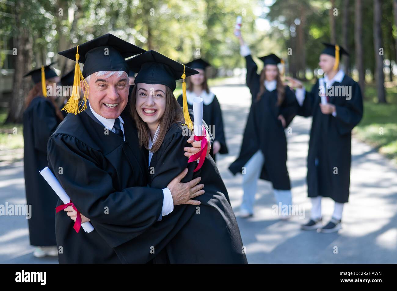 A group of graduates in robes outdoors. An elderly man and a young ...