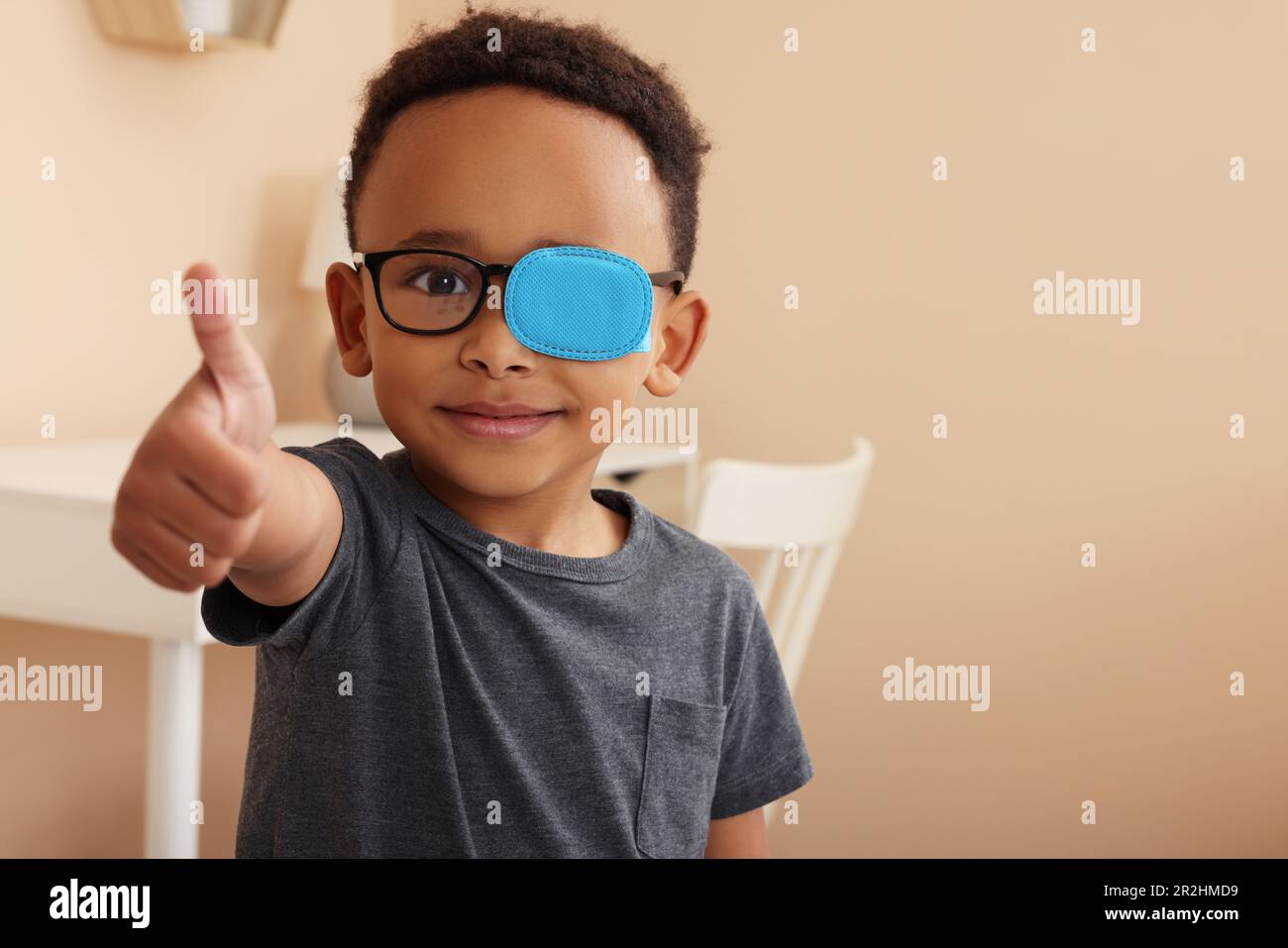 African American boy with eye patch on glasses showing thumb up in room ...