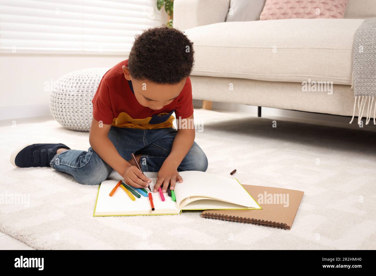 Cute African-American boy drawing in sketchbook with colorful markers ...