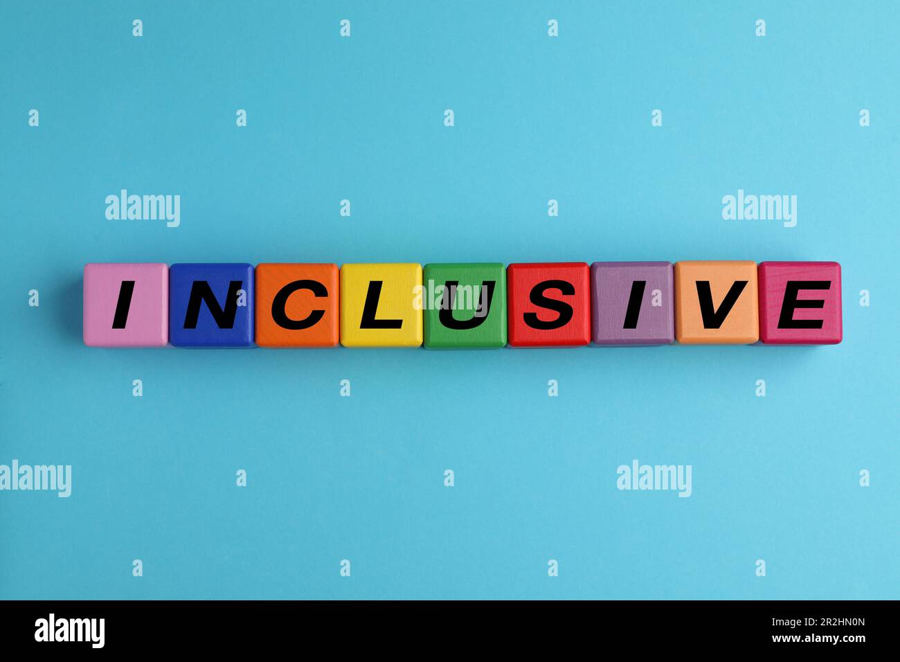 Colorful cubes with word Inclusive on light blue background, flat lay ...
