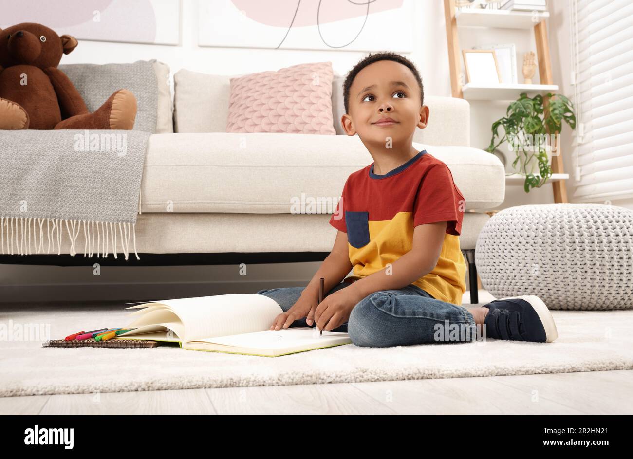 Cute African-American boy drawing in sketchbook with colorful markers ...