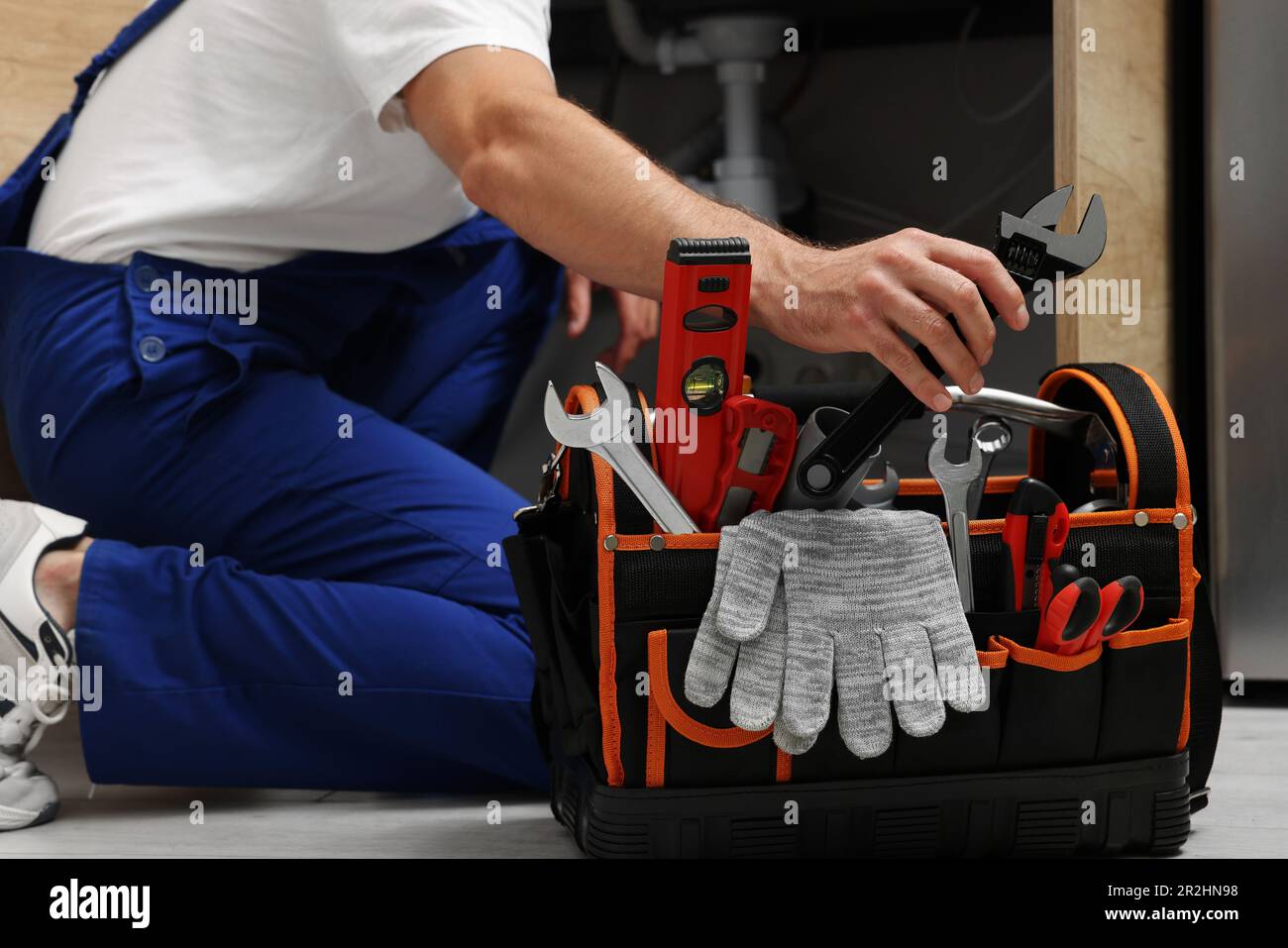 Professional plumber taking adjustable wrench from tool bag indoors ...