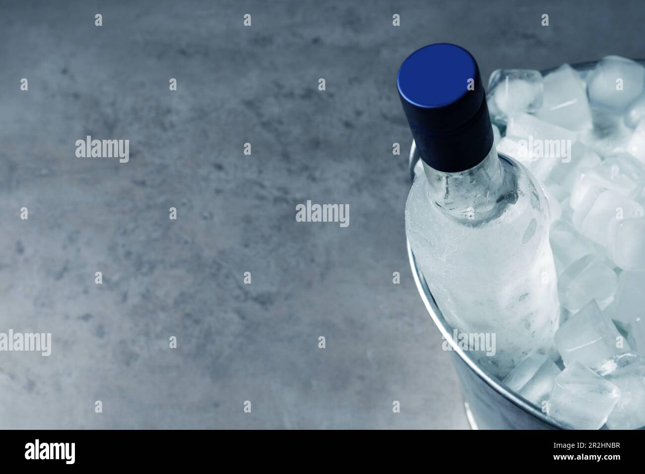 Bottle of vodka in metal bucket with ice on grey table, above view ...