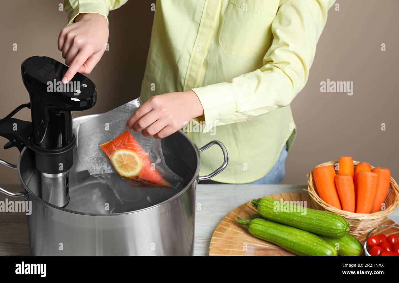 Woman putting vacuum packed salmon into pot and using thermal immersion ...