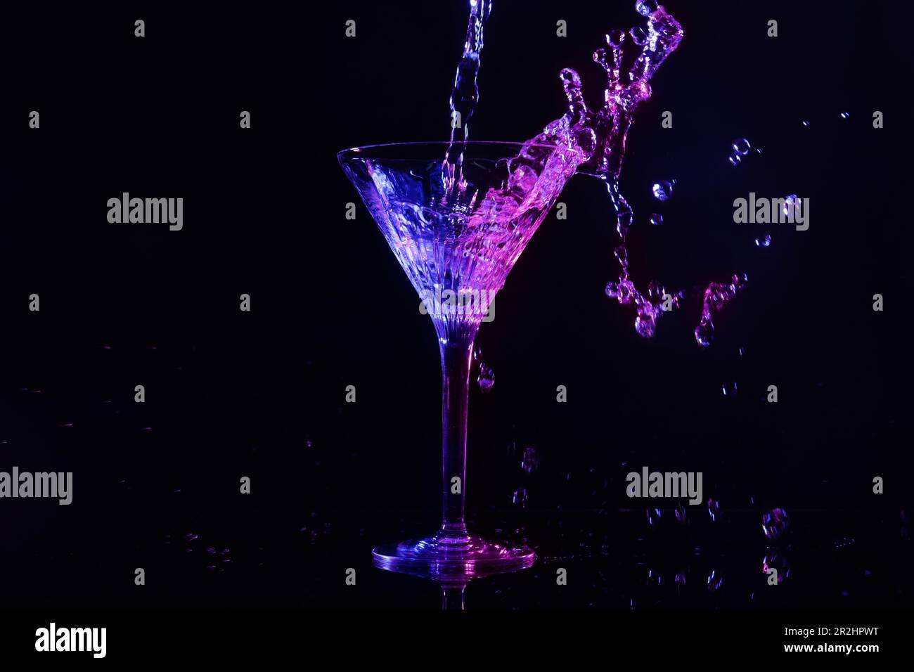Pouring martini. Glass and splashes in neon lights on dark background ...