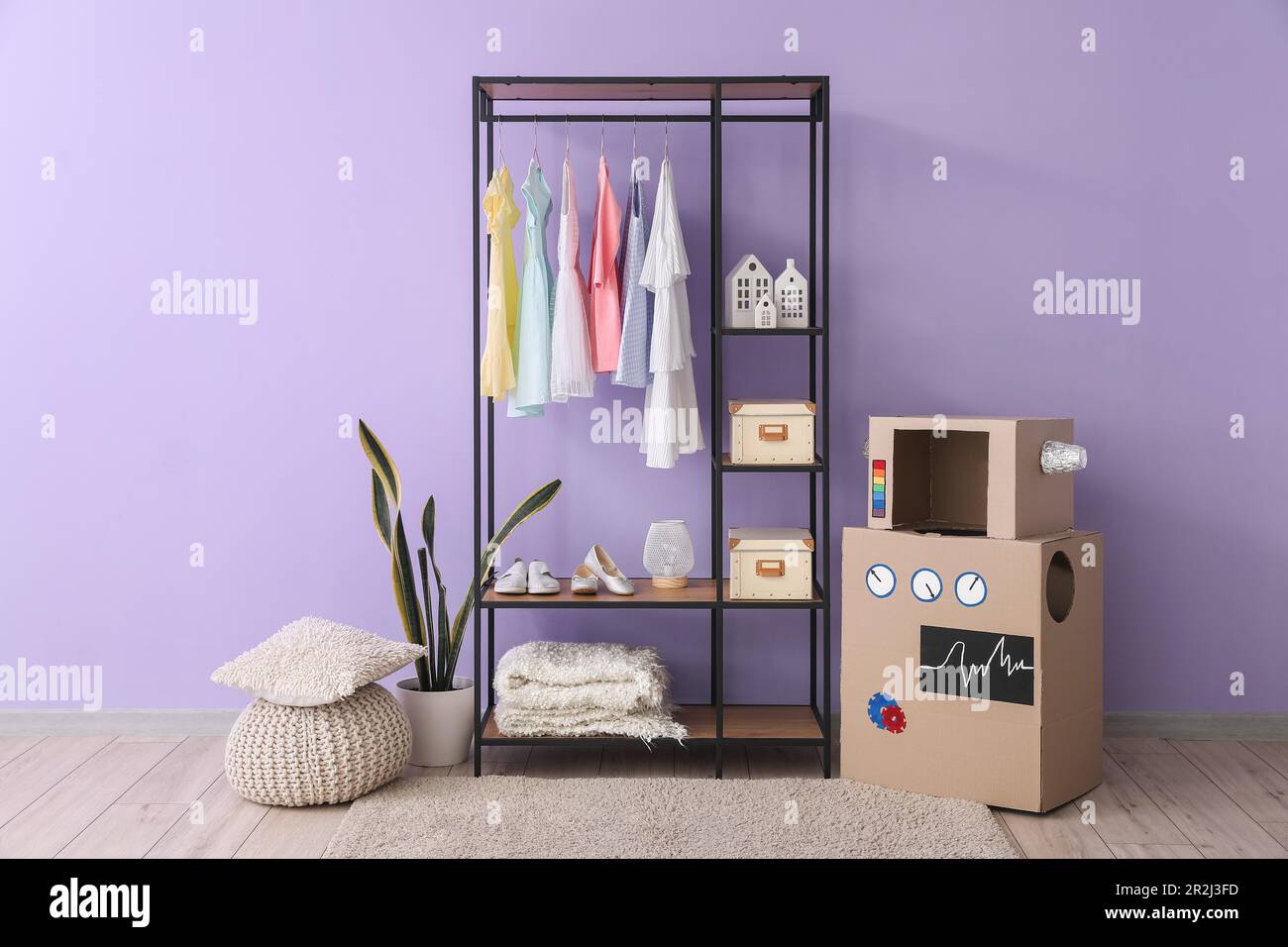 Shelving unit with children's dresses and shoes near lilac wall in room ...