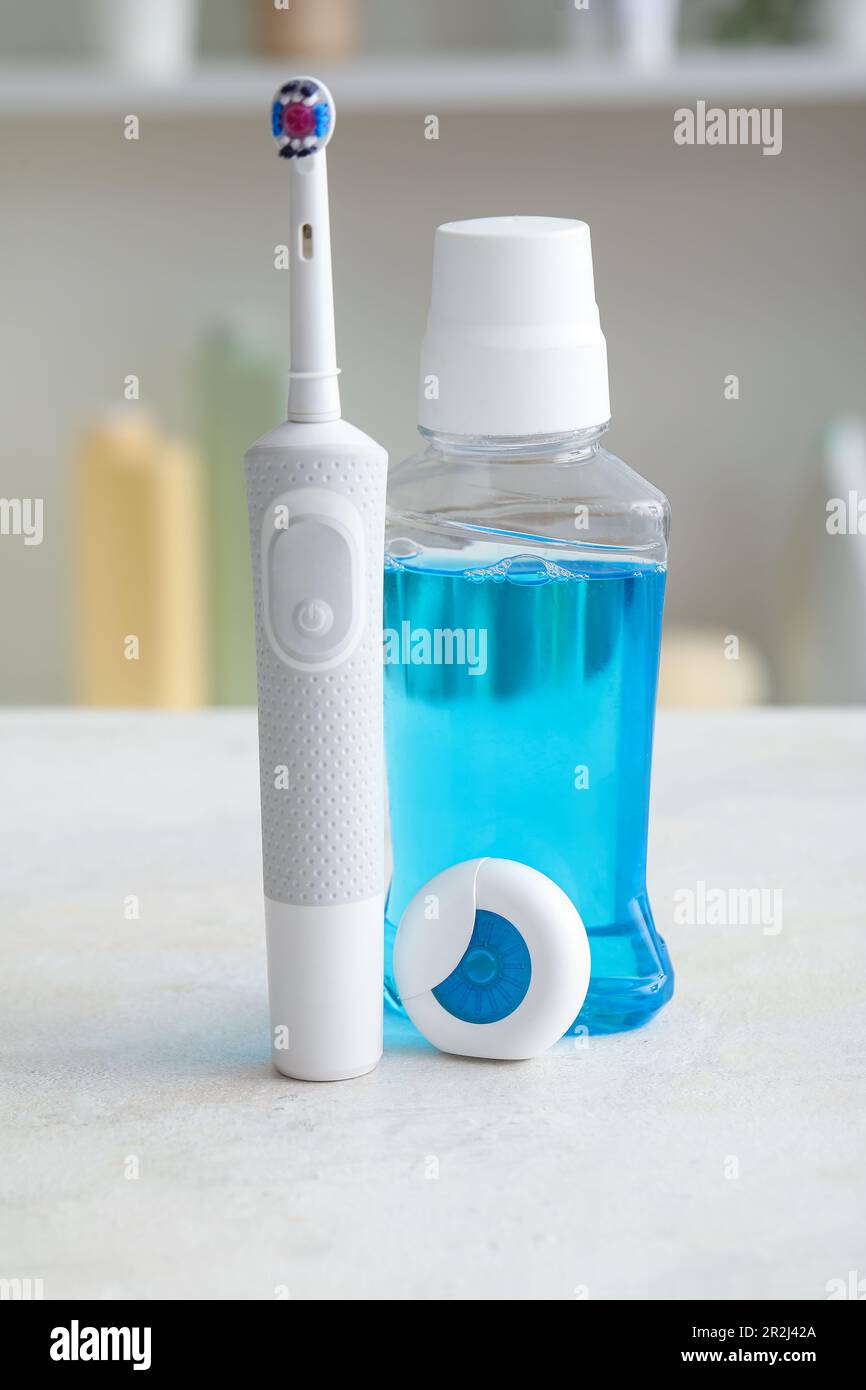 Dental floss with electrical toothbrush and mouthwash on white table in ...