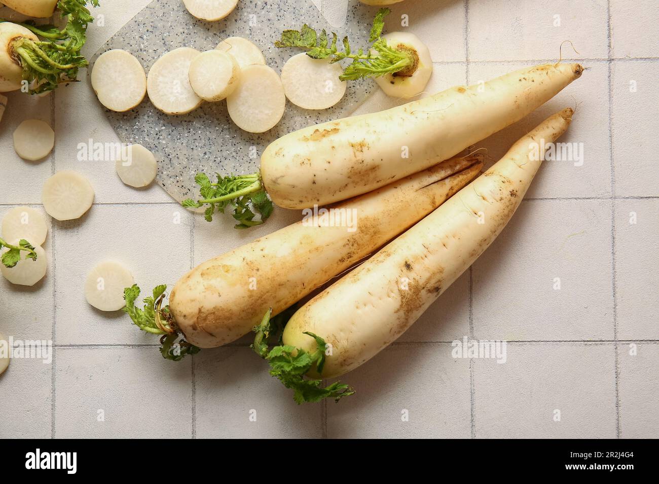 Board with fresh daikon radishes on white tile background Stock Photo ...