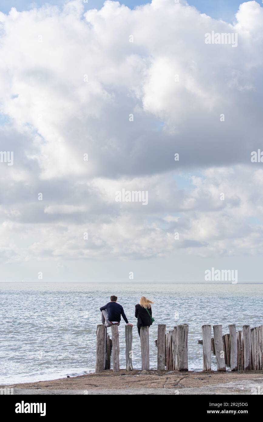 A couple sitting on the wavebreakers of the beach of Groede in the ...