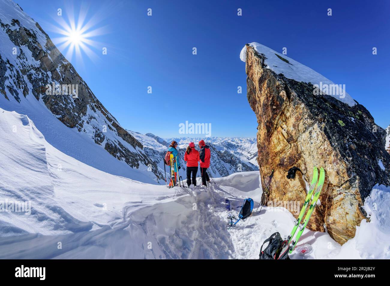 Three people on ski tour stand under rock tower and look at Zillertal ...