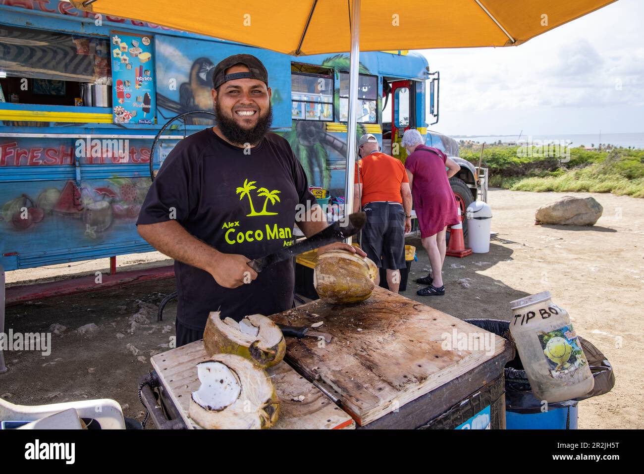 Friendly man opening fresh coconuts at a snack bar in colorful old ...