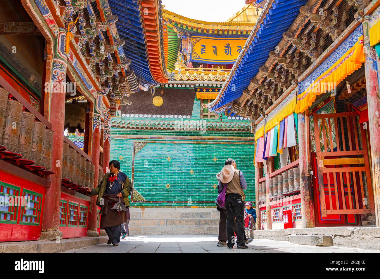 Tibetans walk around a richly decorated temple with prayer wheels and ...