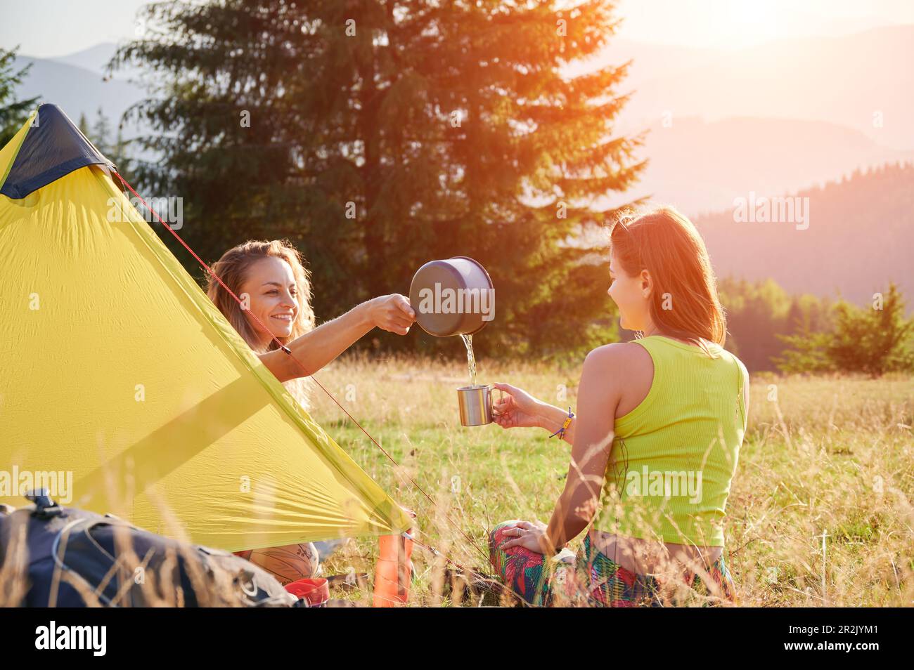 Two women travellers camping outdoors. Young women sitting in campsite ...