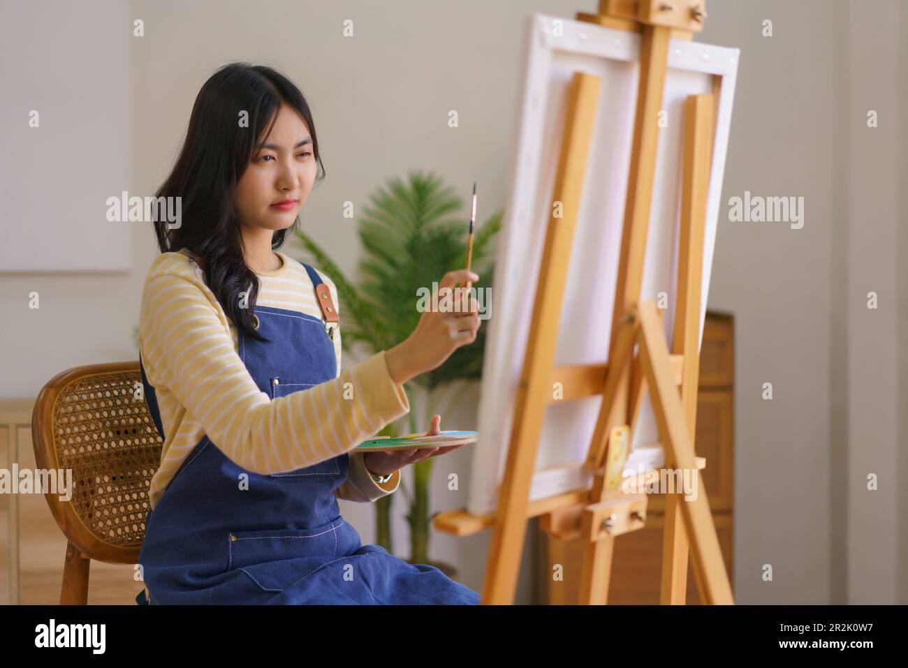 Young woman artist measuring proportion with brush to painting picture ...