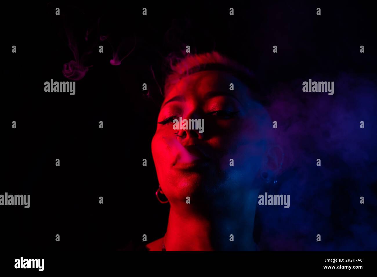 Close up portrait of asian woman with short hair smoking in neon light ...