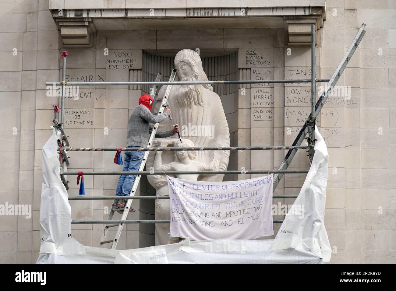 A man wearing a Spiderman mask uses a hammer and chisel to damage the ...