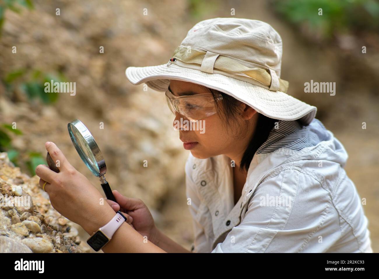 Female geologist using magnifying glass to examine and analyze rock ...