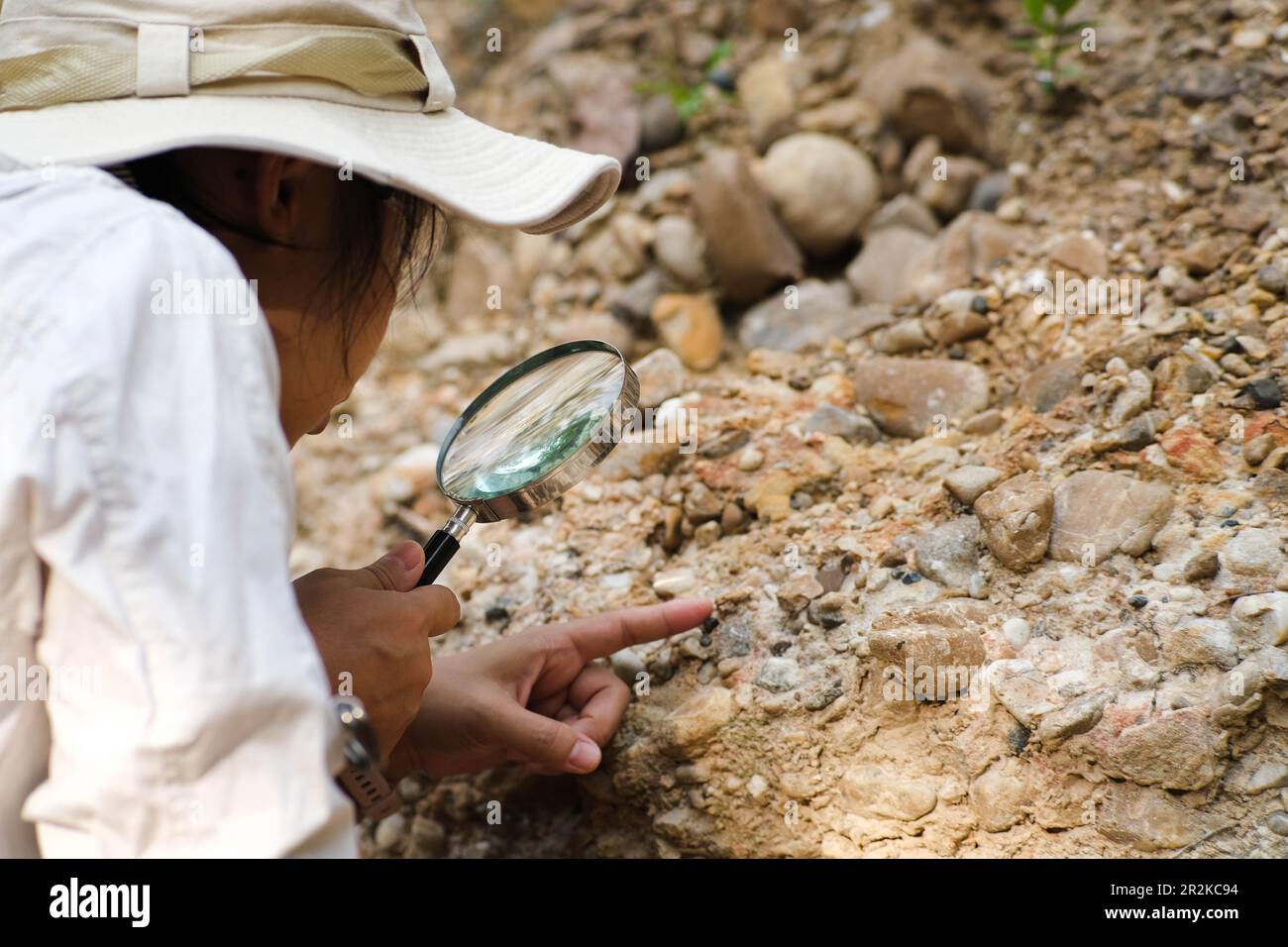 Female geologist using magnifying glass to examine and analyze rock, soil, sand in nature ...