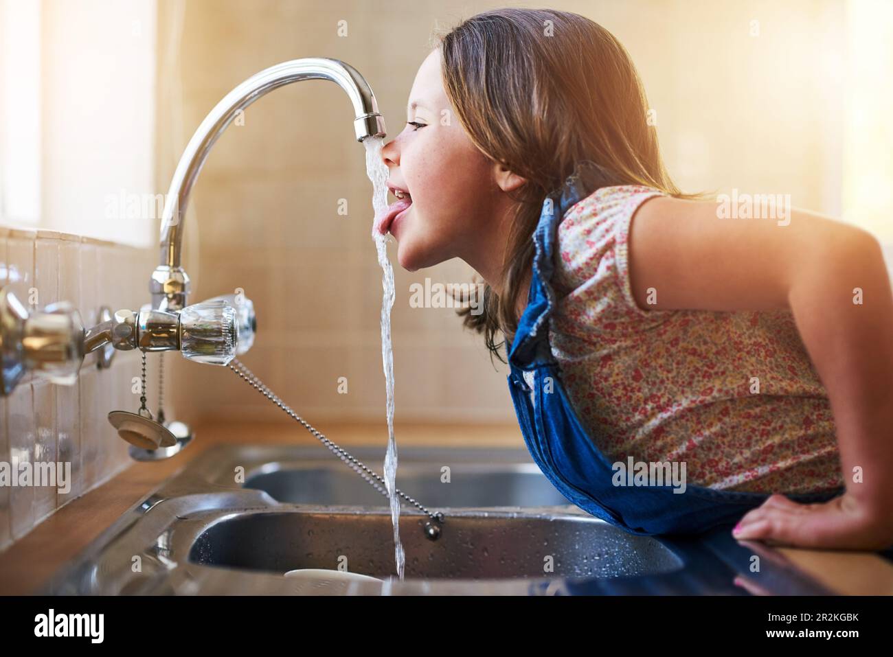 Drinking water, tap and child with tongue out in a home kitchen with a ...