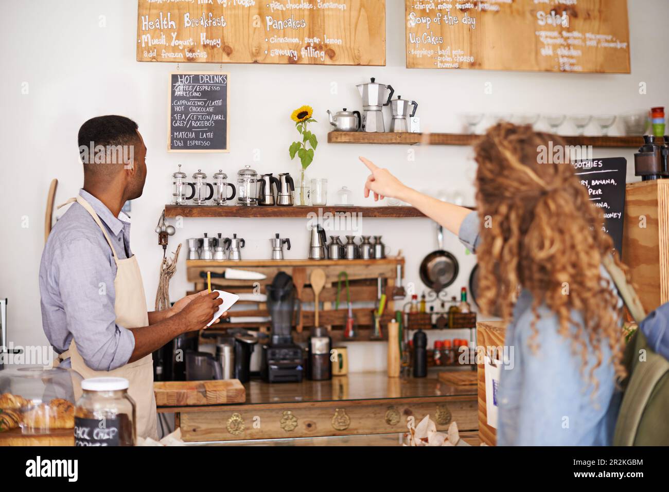 Woman, cafe and pointing at menu on wall with barista, notes and ...